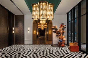 Um hall moderno com piso de padrão geométrico, um lustre central e uma parede com malas empilhadas.