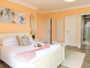 Um quarto com uma cama, uma mesa de cabeceira com abajur, um espelho, um radiador e uma porta que dá para outro cômodo.