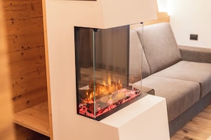 Uma sala de estar moderna com lareira de vidro, piso de madeira e sofá cinzento.