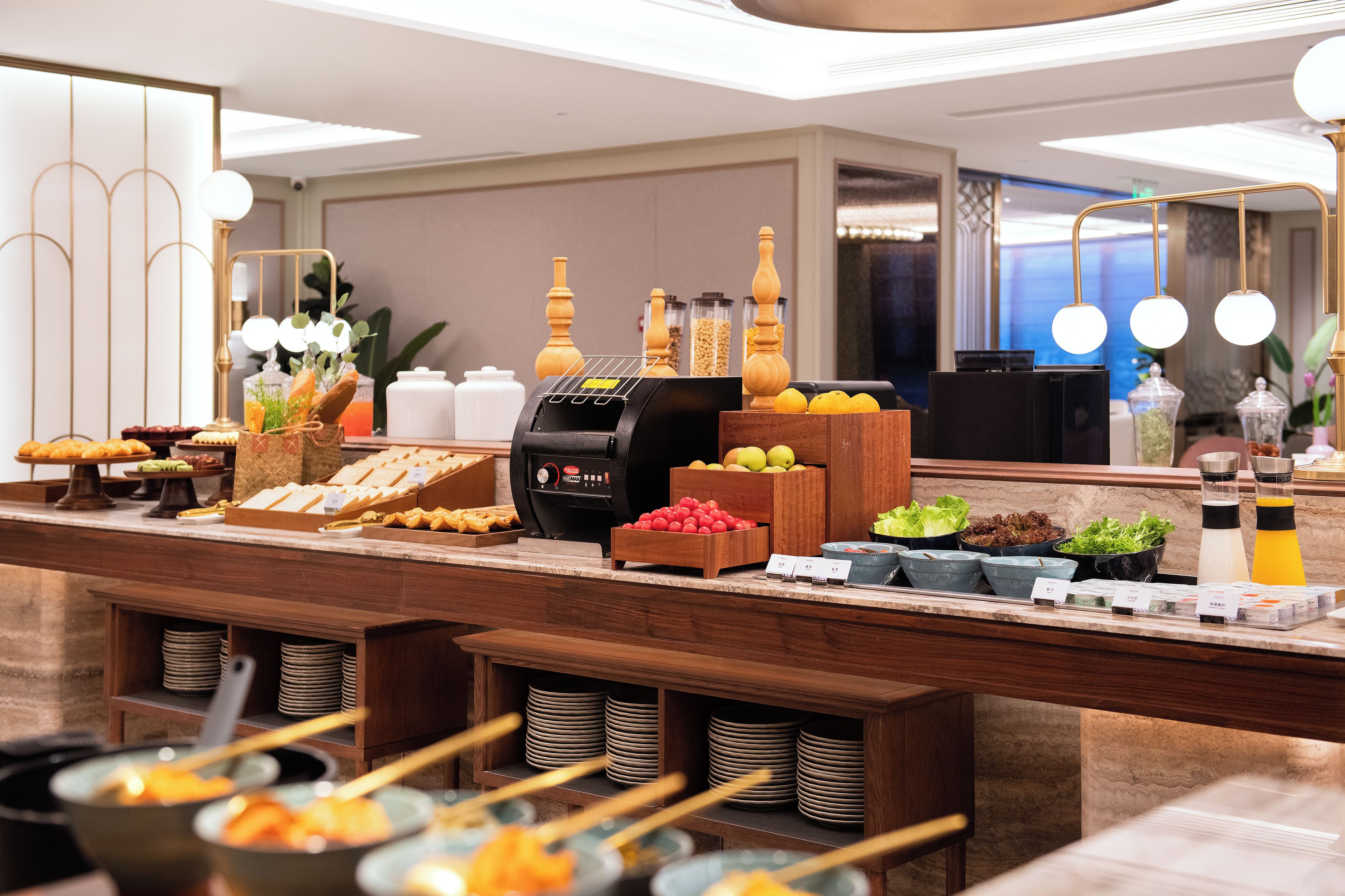 Disposição de buffet com diversos alimentos, máquina de café e acompanhamentos.
