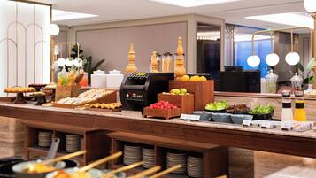 Disposição de buffet com diversos alimentos, máquina de café e acompanhamentos.
