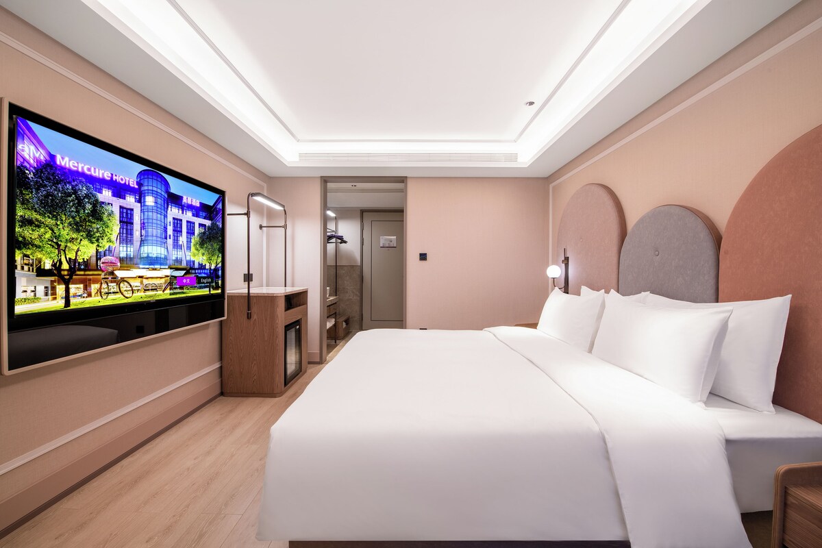 Quarto de hotel com uma cama grande, televisão fixada na parede e um armário de madeira.