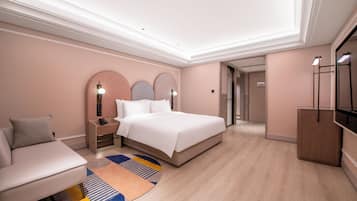 Quarto de hotel moderno com cama grande, mesas de cabeceira, sofá e televisão.