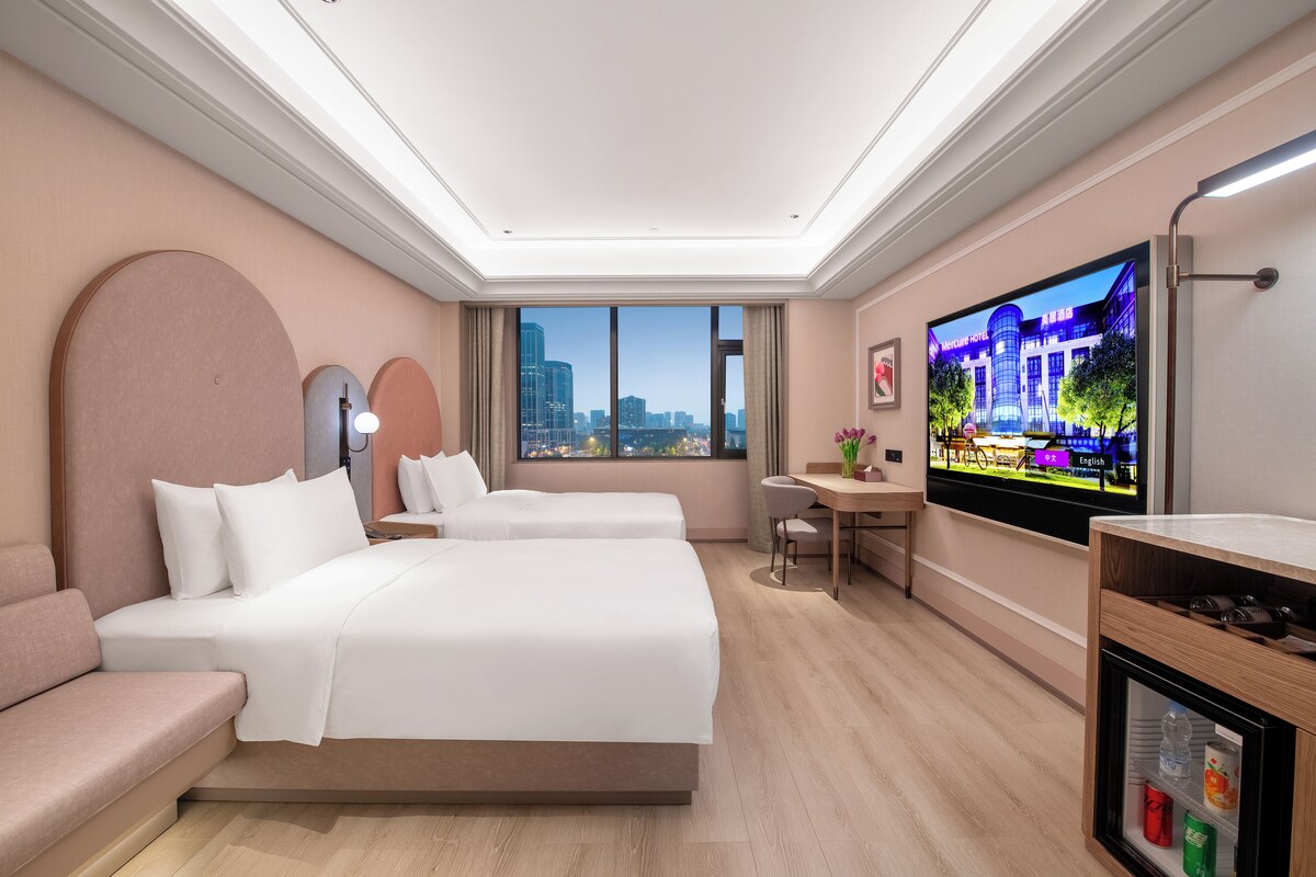 Quarto de hotel com duas camas, uma escrivaninha, televisão e minibar.