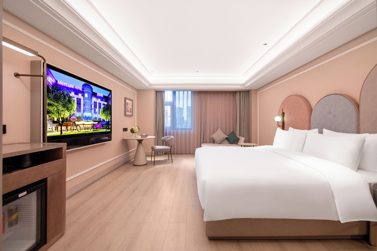 Quarto de hotel com cama grande, televisão na parede, mesa pequena e uma cadeira.