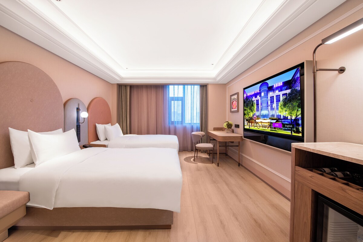 Quarto de hotel com duas camas, televisão, escrivaninha e uma cadeira.
