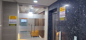 A hotel entrance with a glass door, a signboard with room details, and a marble wall.