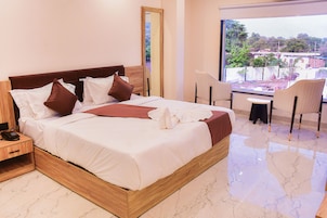 Quarto de hotel com uma cama grande, uma mesa de cabeceira com telefone, uma cadeira, uma mesinha e vista para o exterior.