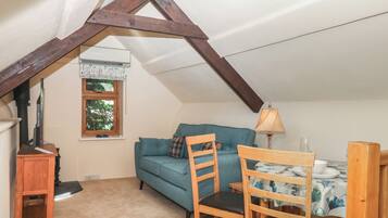 Um quarto de sótão acolhedor, com teto inclinado, um sofá azul, uma mesa de jantar de madeira e um pequeno aquecedor de madeira.