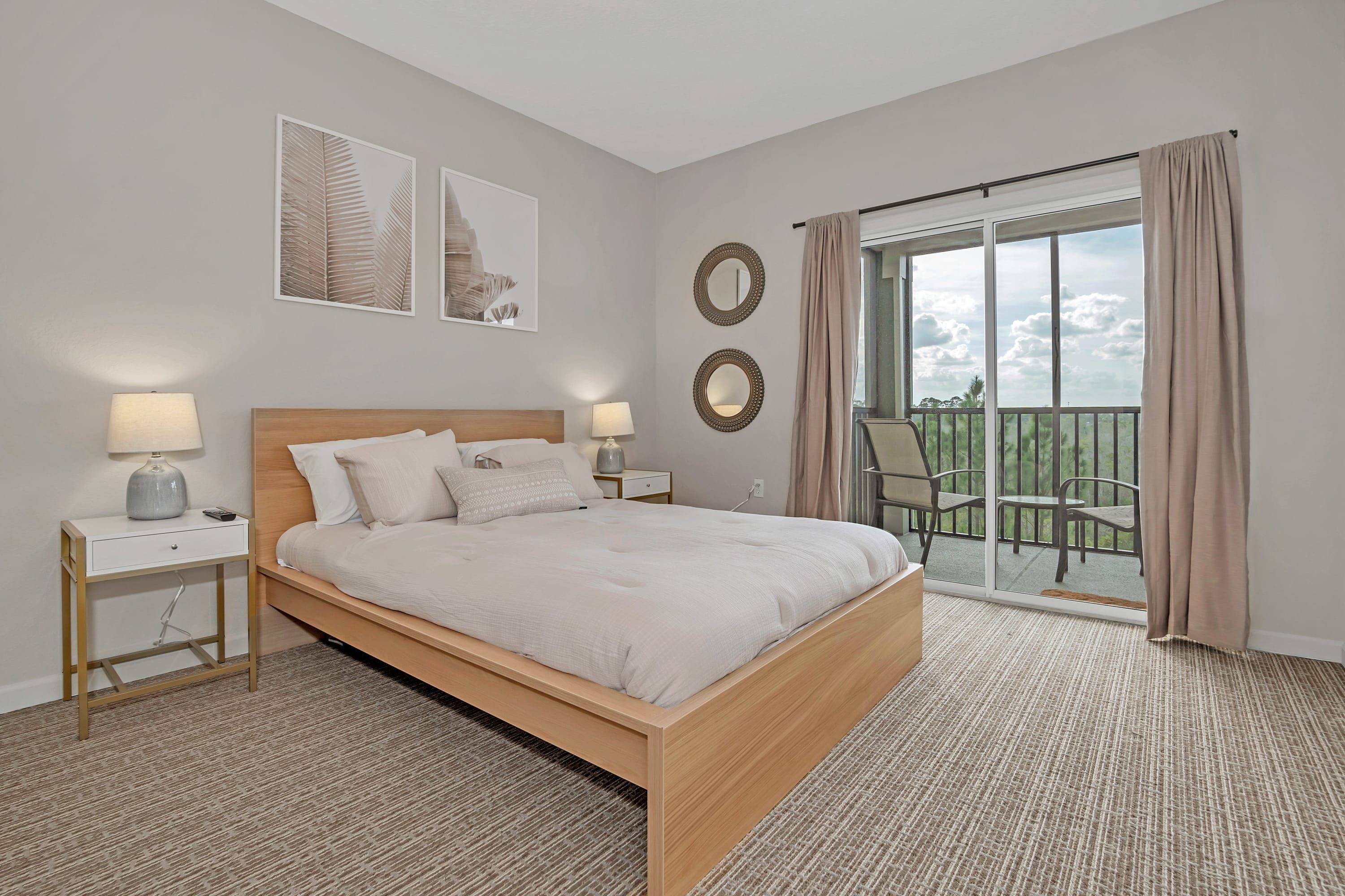 Quarto de hotel com uma cama, duas mesinhas de cabeceira, um criado-mudo, uma varanda com vista e dois espelhos fixados na parede.