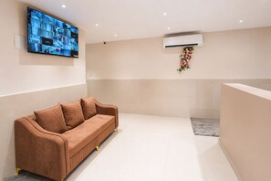 Um interior moderno com sofá, televisão na parede, aparelho de ar condicionado e um arranjo floral decorativo.