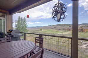 Uma varanda com mesa e cadeiras, churrasqueira, luminária pendente e vista para um campo de golfe.