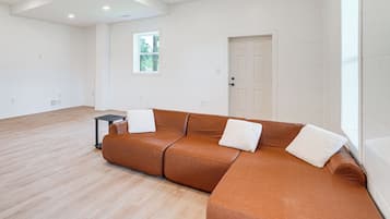 Um quarto espaçoso com um sofá de couro marrom, uma pequena mesa lateral preta e uma janela com vista para o verde.