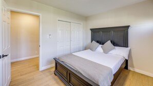 Quarto com cama de madeira, paredes brancas e porta que dá para outro cômodo.