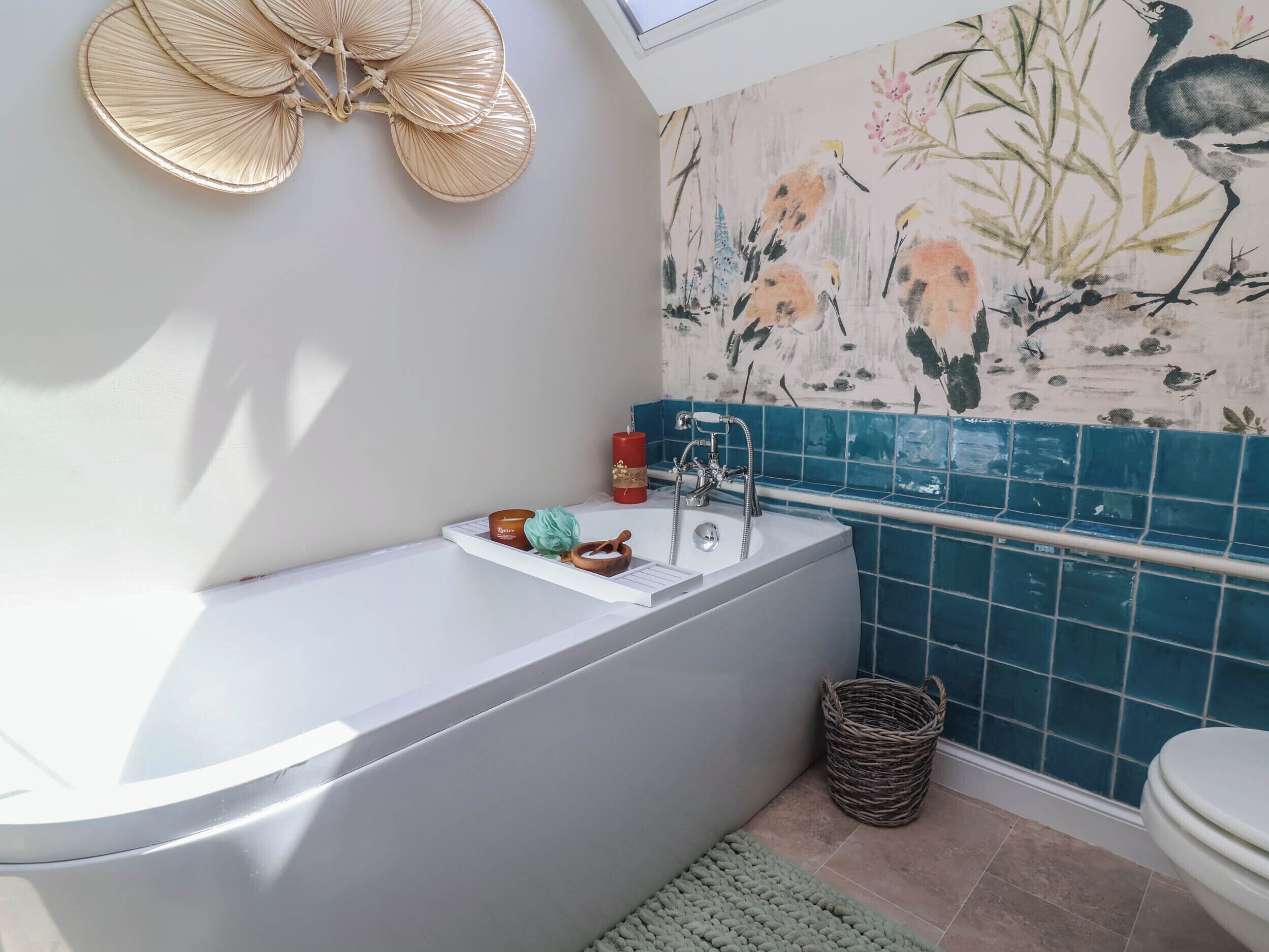 Um banheiro com banheira, chuveiro, vaso sanitário e parede com um mural floral.