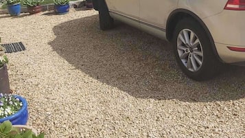 Um carro bege estacionado em cascalho, com casas ao fundo.