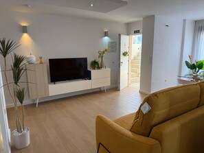 Uma sala de estar moderna com uma televisão de tela plana, um sofá e uma área de jantar com uma mesa de vidro.