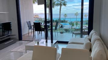 Sala de estar moderna com uma grande porta de vidro deslizante que dá para uma varanda com vista para o mar e palmeiras.