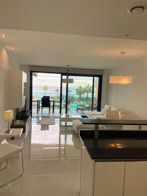 Quarto de hotel moderno com uma grande porta de vidro deslizante que dá para uma varanda com piscina e palmeiras.