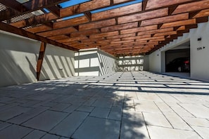 Uma área externa coberta com piso de azulejos, vigas de madeira no teto e uma placa indicando uma piscina.