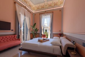 Quarto de hotel com cama grande, sofá, televisão e mesa de jantar com bandeja de café da manhã.