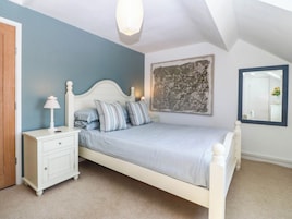 Quarto com cama, mesa de cabeceira e espelho fixado na parede.