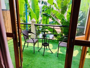 Varanda com mesa e cadeiras, cercada por folhagem exuberante.