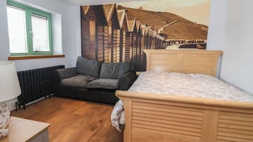 Quarto com cama, sofá, radiador, janela com persianas e um mural na parede.