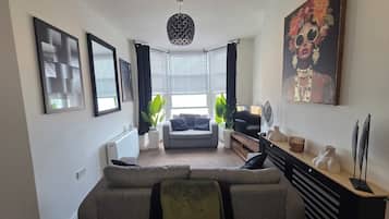 Uma sala de estar com um sofá, uma televisão e um quadro grande na parede.