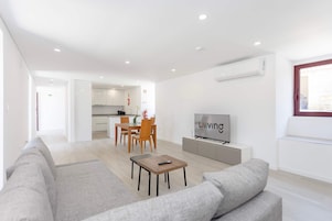 Uma sala de estar moderna com um sofá, uma televisão e um espaço de refeições com cadeiras e uma mesa.
