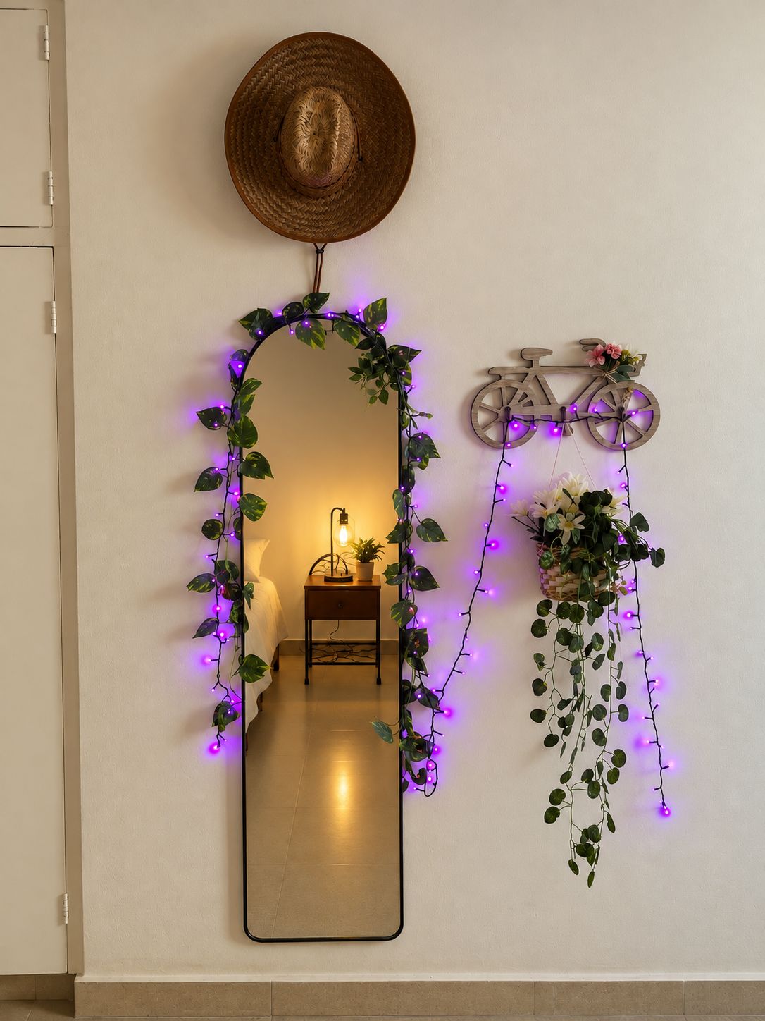Um espelho com moldura de madeira, envolto em luzes roxas e vegetação, decorado com uma bicicleta e um chapéu em cima.