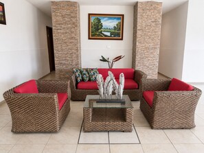Um quarto com mobiliário de vime, almofadas vermelhas, uma mesa de centro de vidro e um quadro na parede.