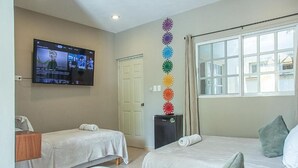 Quarto de hotel com duas camas, televisão fixada na parede, porta e janela com cortinas.