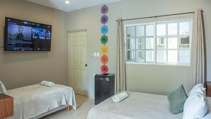 Quarto de hotel com duas camas, televisão fixada na parede, janela com cortinas e um enfeite de parede decorativo.
