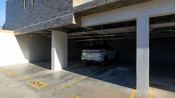 Um estacionamento com vagas demarcadas, um carro branco estacionado e um edifício com paredes e colunas revestidas de azulejos.