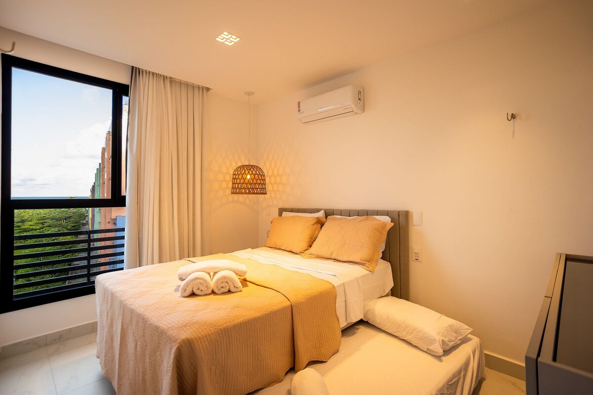 Quarto de hotel com cama, janela com cortinas, ar condicionado fixado na parede e vista para prédios.