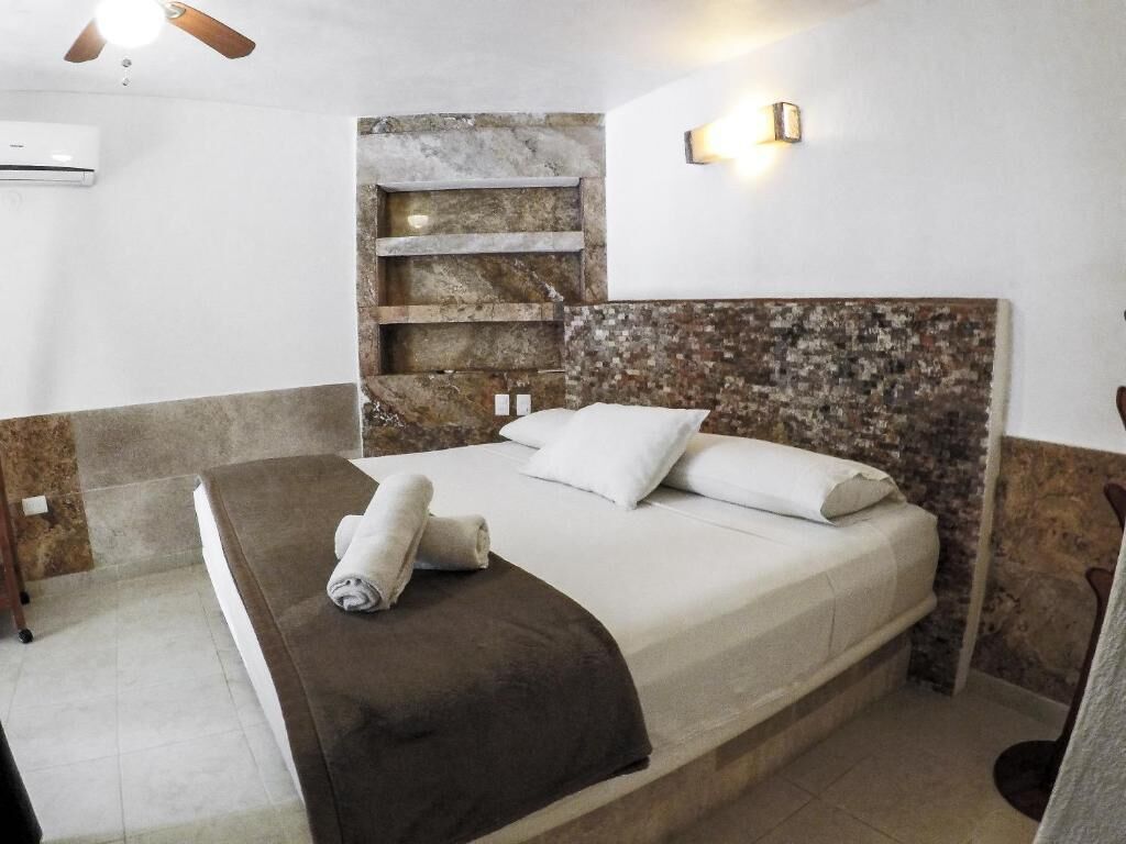 Quarto com uma cama, cabeceira, prateleira na parede e ventilador de teto.