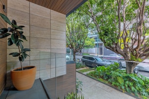 Um edifício moderno com fachada em azulejos, um vaso de planta e vista para carros estacionados e árvores.