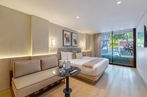 Quarto de hotel moderno com uma cama, um sofá, uma mesinha e uma janela ampla com vista para o exterior.
