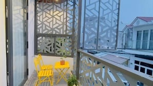 Uma varanda com guarda-corpo de padrão geométrico, uma cadeira amarela, uma mesa pequena e plantas em vasos.