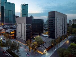 Uma área urbana moderna com edifícios altos, uma passarela para pedestres e uma rua com veículos.