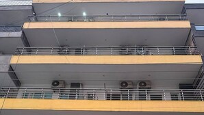 Um edifício com várias andares, varandas, aparelhos de ar condicionado e portão fechado.