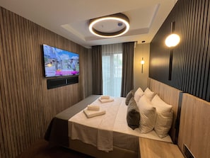 Quarto de hotel com cama, televisão de tela plana na parede e luminária no teto.