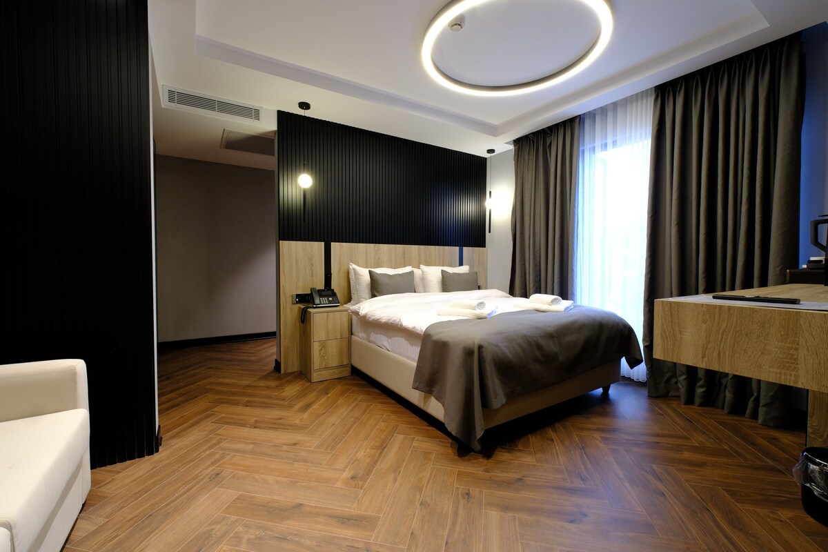 Quarto de hotel moderno com uma cama grande, mesas de cabeceira, uma escrivaninha e vista para o exterior.