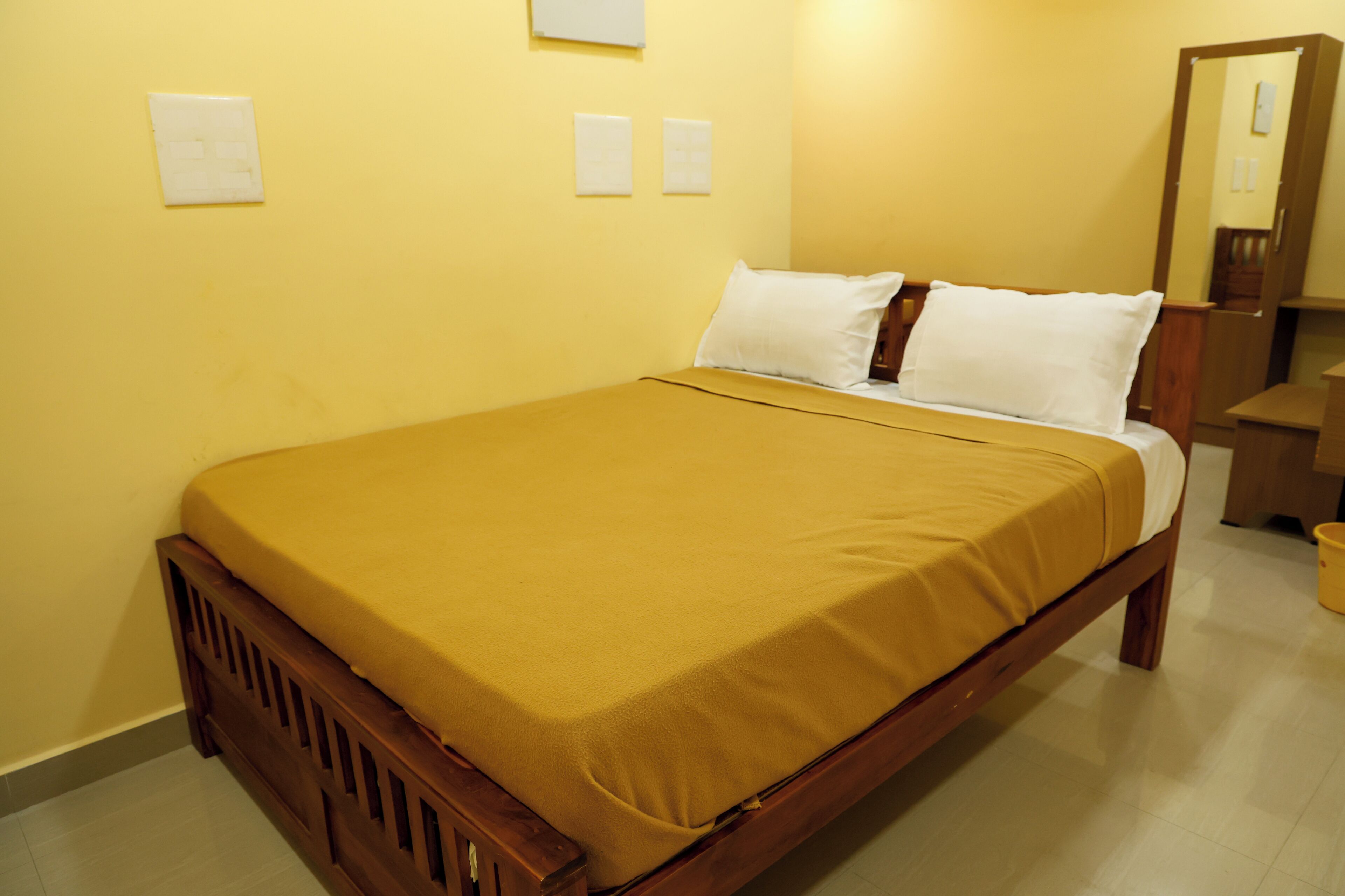 Cama com estrutura de madeira, colcha amarela e almofadas brancas.