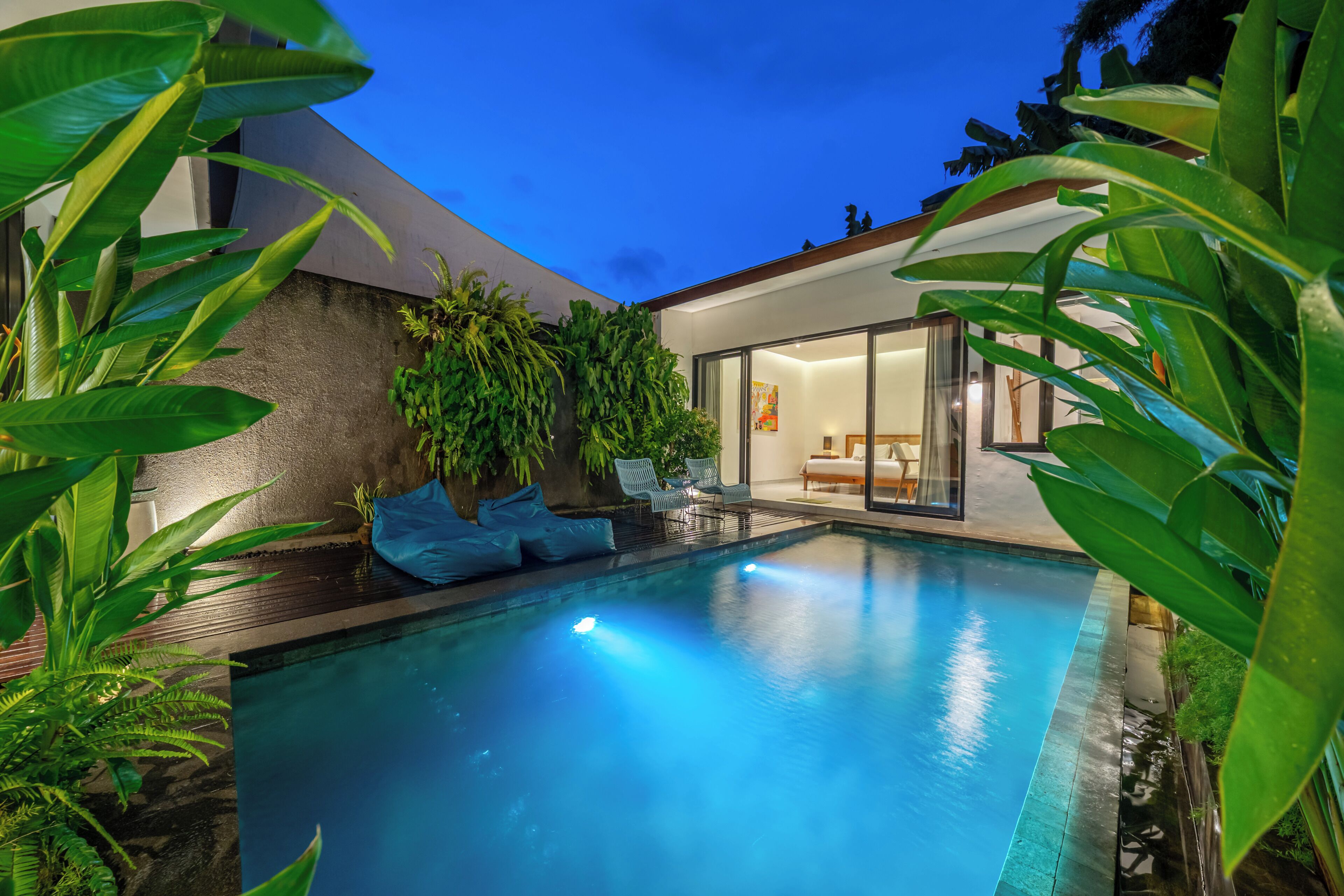 Uma área de piscina moderna com um lounge envidraçado, cercada por vegetação exuberante.