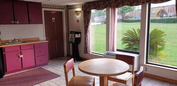 Uma cozinha com mesa e cadeiras, uma janela com vista para uma área gramada e uma porta com um aviso.