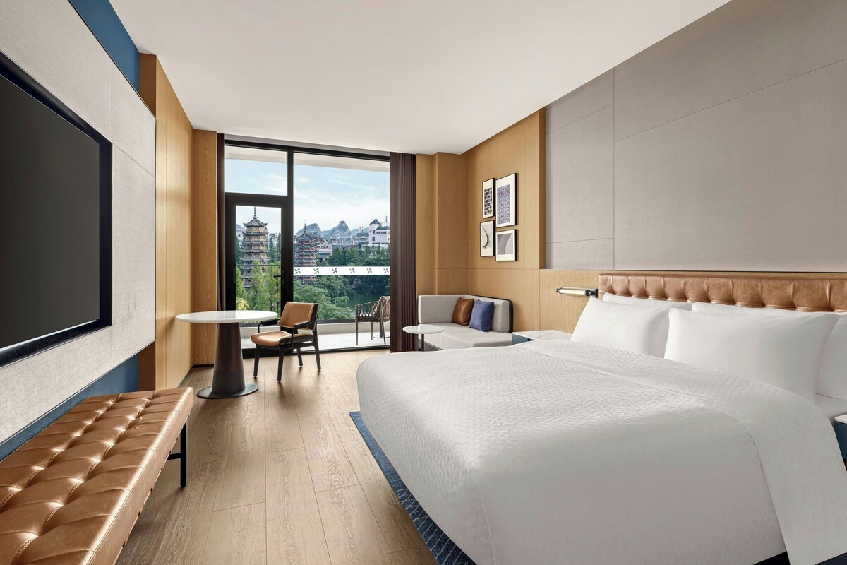 Quarto de hotel com uma cama grande, área de estar com mesa e cadeiras, e vista para uma pagoda tradicional pela janela.