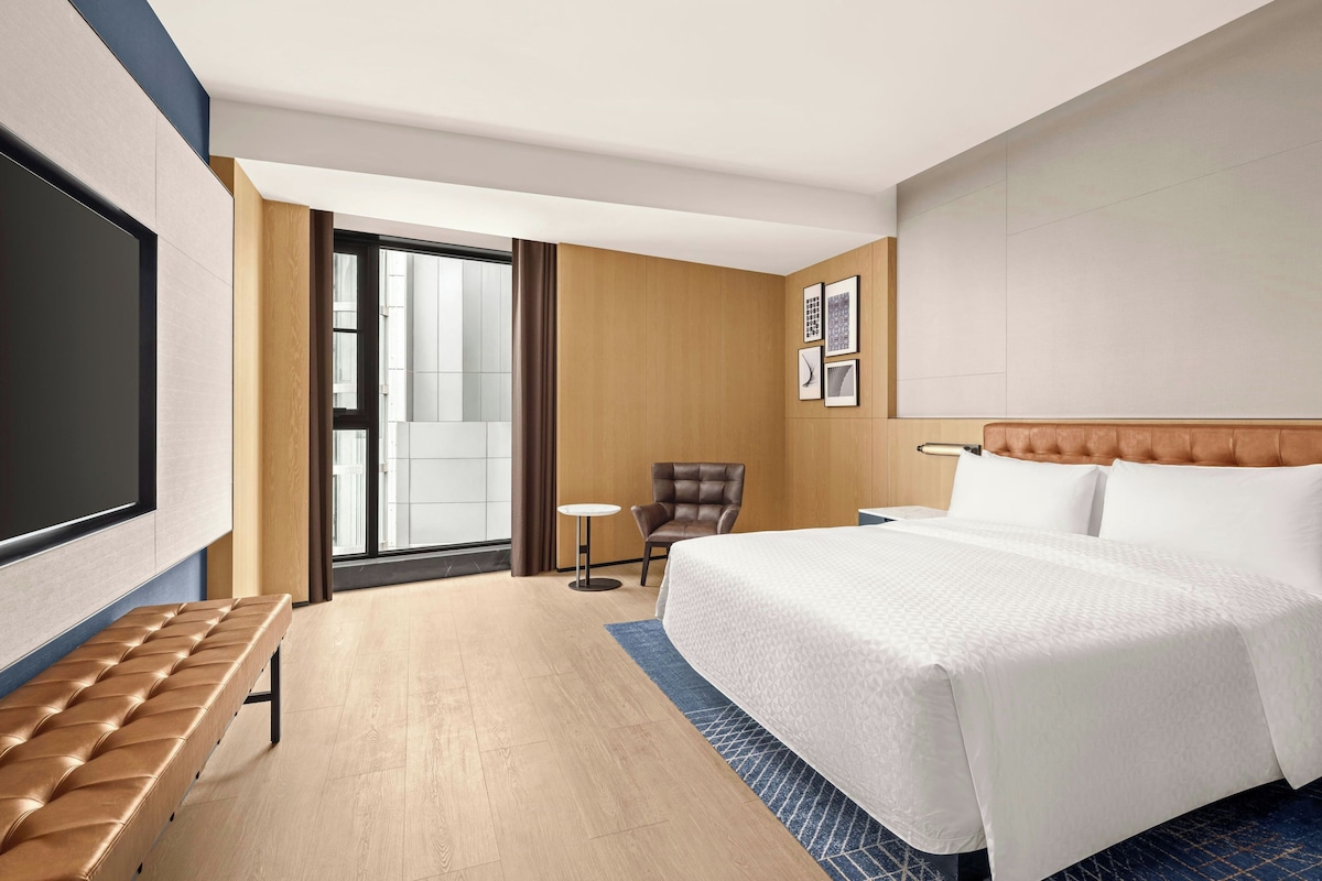 Quarto de hotel com cama, área de estar, televisão e janela.