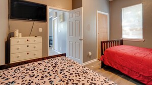 A bedroom with a bed, a dresser, a television, and a door leading to another room.